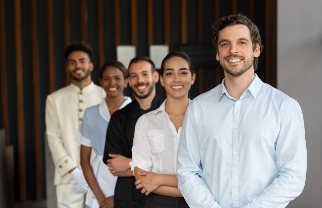 Hotel manager and his team standing behind all looking at camera ...